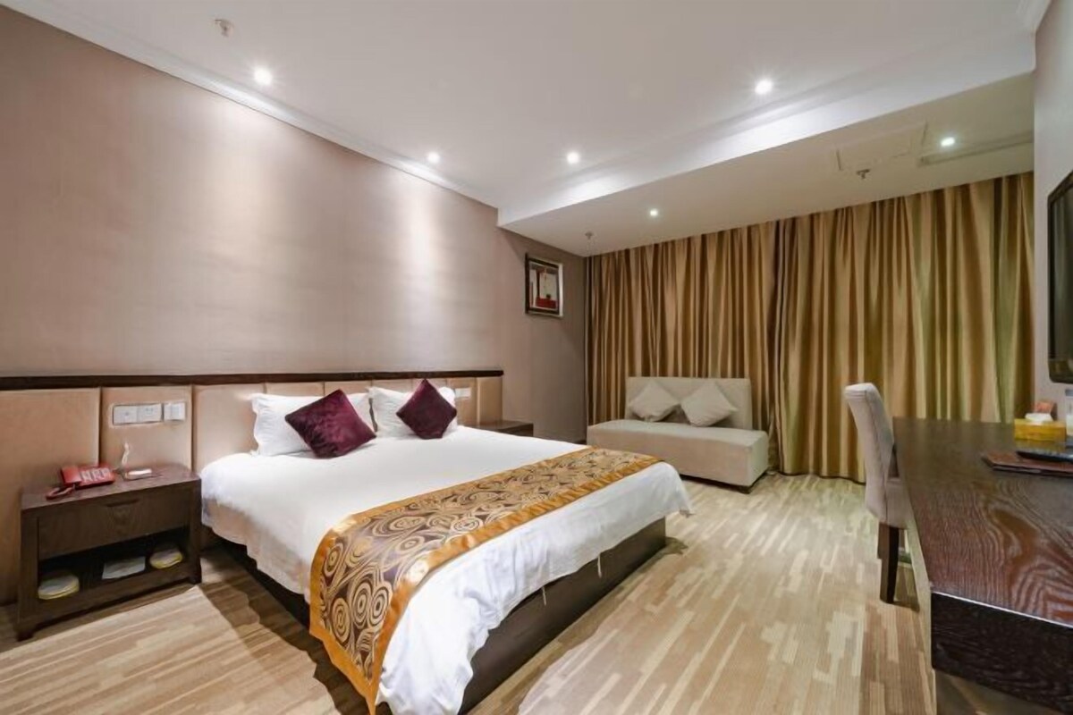 Quarto de hotel com uma cama grande, uma mesa de cabeceira, uma cadeira, um sofá e uma mesa de madeira.