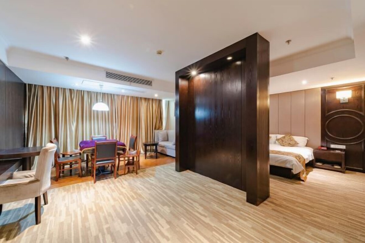 Quarto de hotel com cama, escrivaninha, cadeira, mesa pequena e abajur.