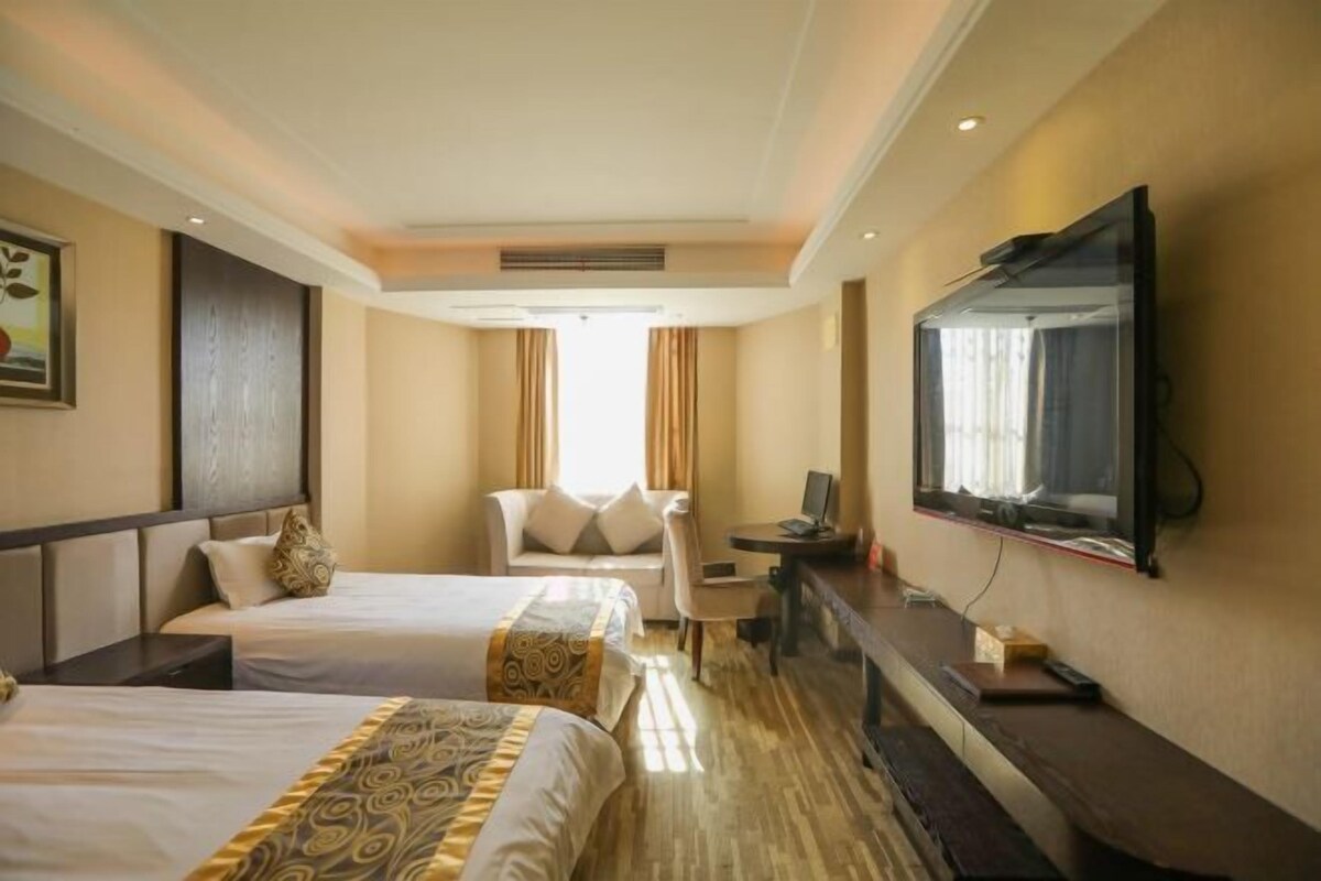 Quarto de hotel com duas camas, uma escrivaninha, uma cadeira, televisão e uma janela grande.
