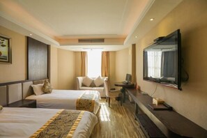 Quarto de hotel com duas camas, uma escrivaninha, uma cadeira, televisão e uma janela grande.