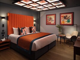 Quarto de hotel moderno com uma cama grande, uma escrivaninha, uma cadeira e obras de arte nas paredes.