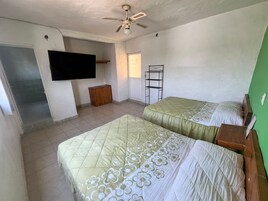 Quarto com duas camas, um ventilador de teto, uma TV fixada na parede e um pequeno armário de madeira.
