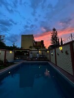 Uma piscina com vista para o pôr do sol, um edifício com telhado plano e uma cerca de arame farpado.