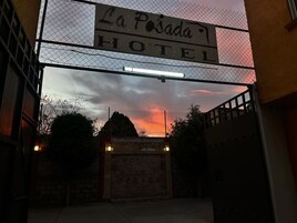A entrada do Hotel La Posada, com uma placa sobre o portão e um pôr do sol ao fundo.