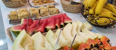 Uma mesa de buffet com diversas frutas, doces e um bolo.