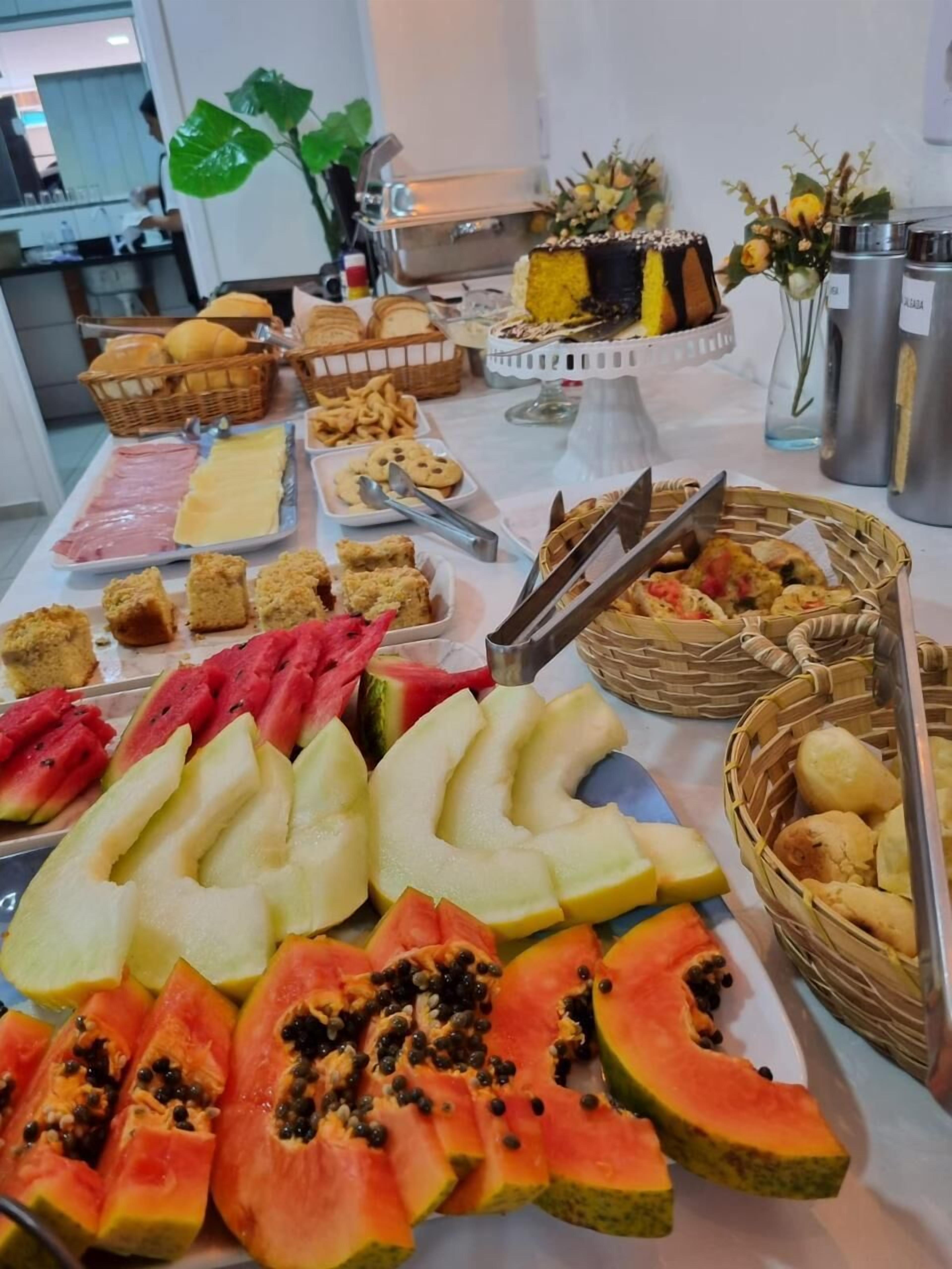 Uma mesa de buffet com diversos alimentos, incluindo frutas, doces e sobremesas.