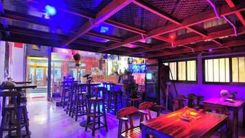 Uma área de bar com banquetas e mesas, um balcão e vista para a rua.