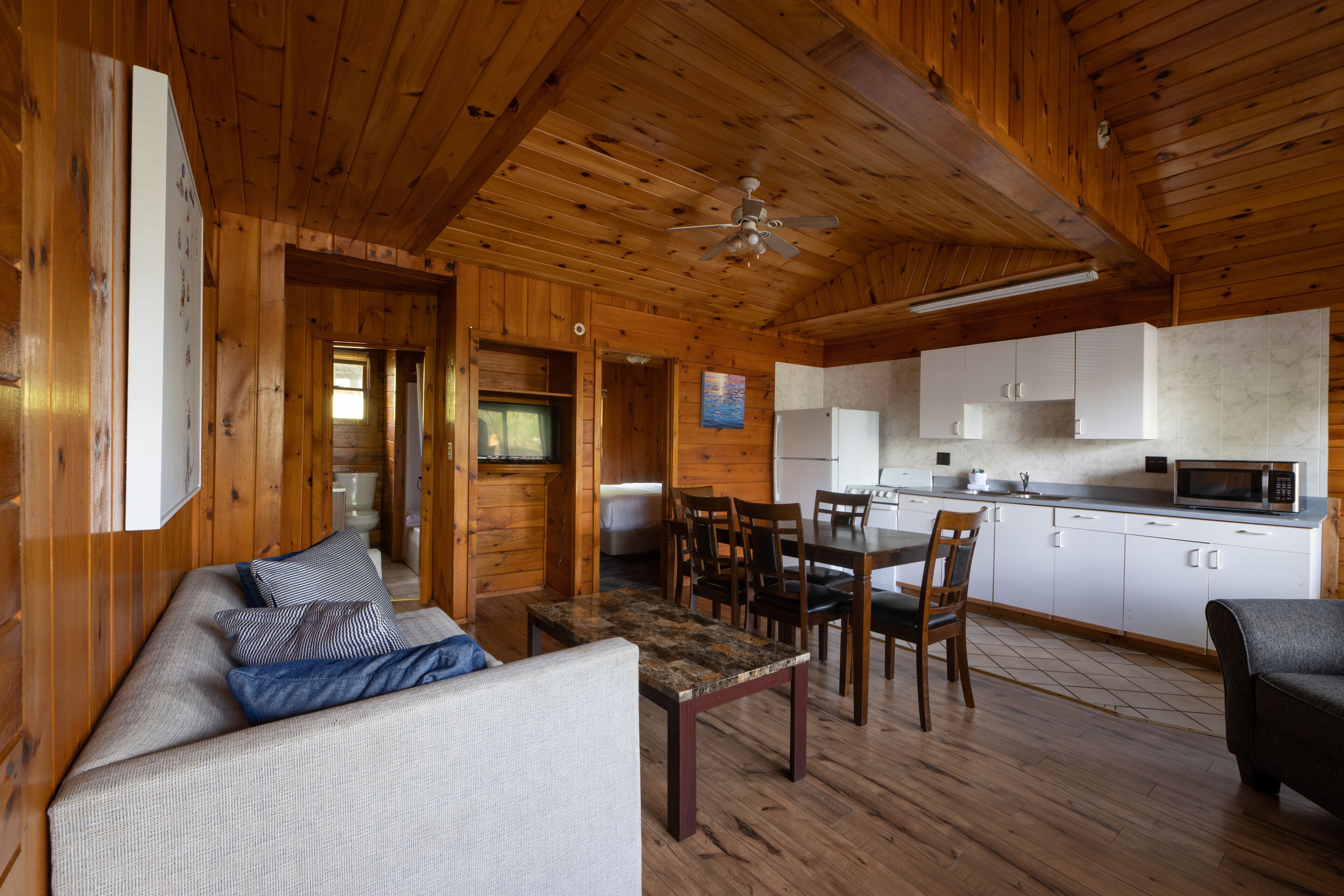 Interior de madeira com sala de jantar, cozinha e um sofá com almofadas.