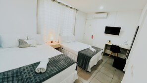 Quarto de hotel com duas camas, uma escrivaninha, uma cadeira, uma televisão e ar condicionado.