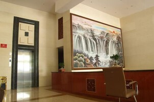 Um hall com balcão de recepção, uma grande pintura de uma cascata, um elevador e uma cadeira.