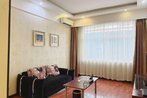 Uma sala de estar com um sofá preto, uma mesinha e uma janela grande com cortinas.