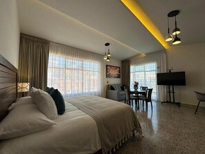 Quarto de hotel com uma cama grande, uma escrivaninha com cadeira, televisão e janela com cortinas.