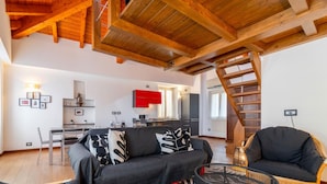 Ampla sala de estar com teto alto, vigas de madeira, cozinha moderna e escada.