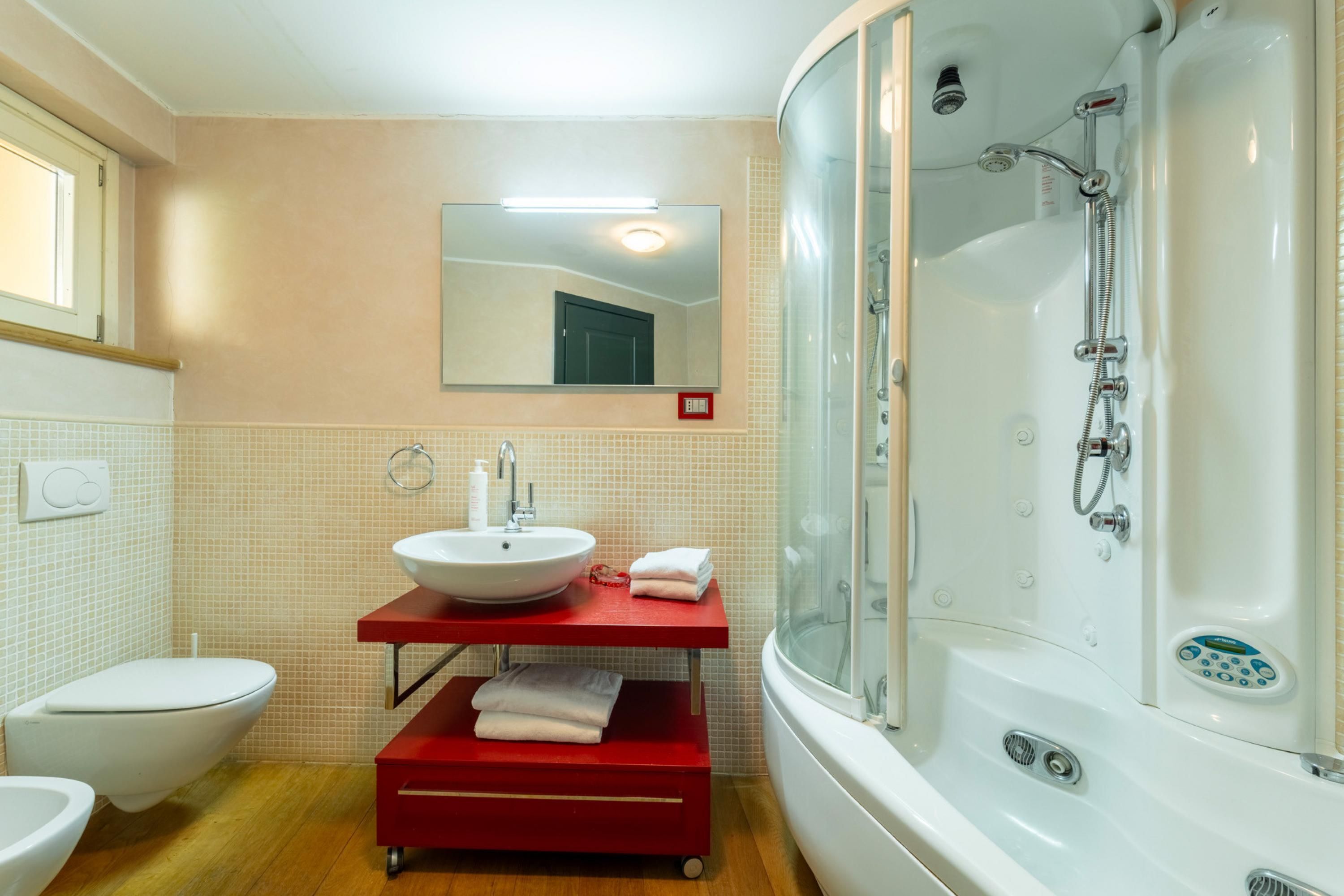 Um banheiro moderno com uma banheira branca, um lavatório vermelho, um vaso sanitário branco e um chuveiro com paredes de vidro.