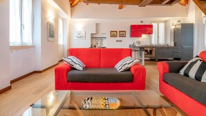 Uma sala de estar com um sofá vermelho, uma mesa de centro de vidro e uma cozinha ao fundo.