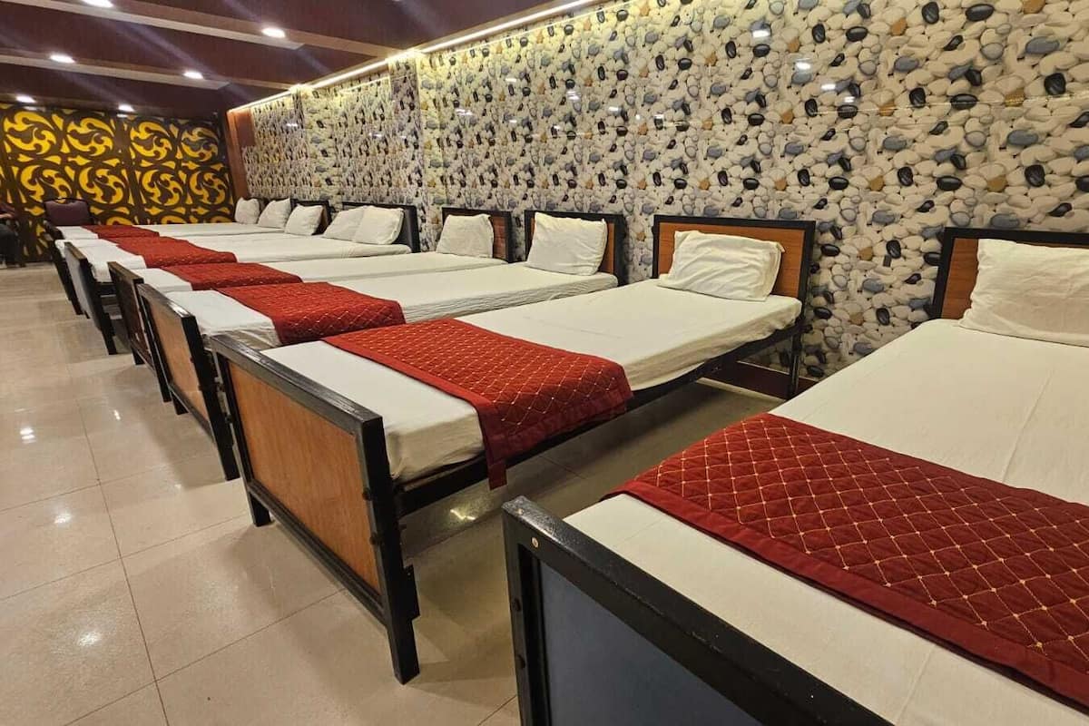 Quarto de hotel com várias camas dispostas em linha, cada uma com estrutura de madeira e roupa de cama branca.