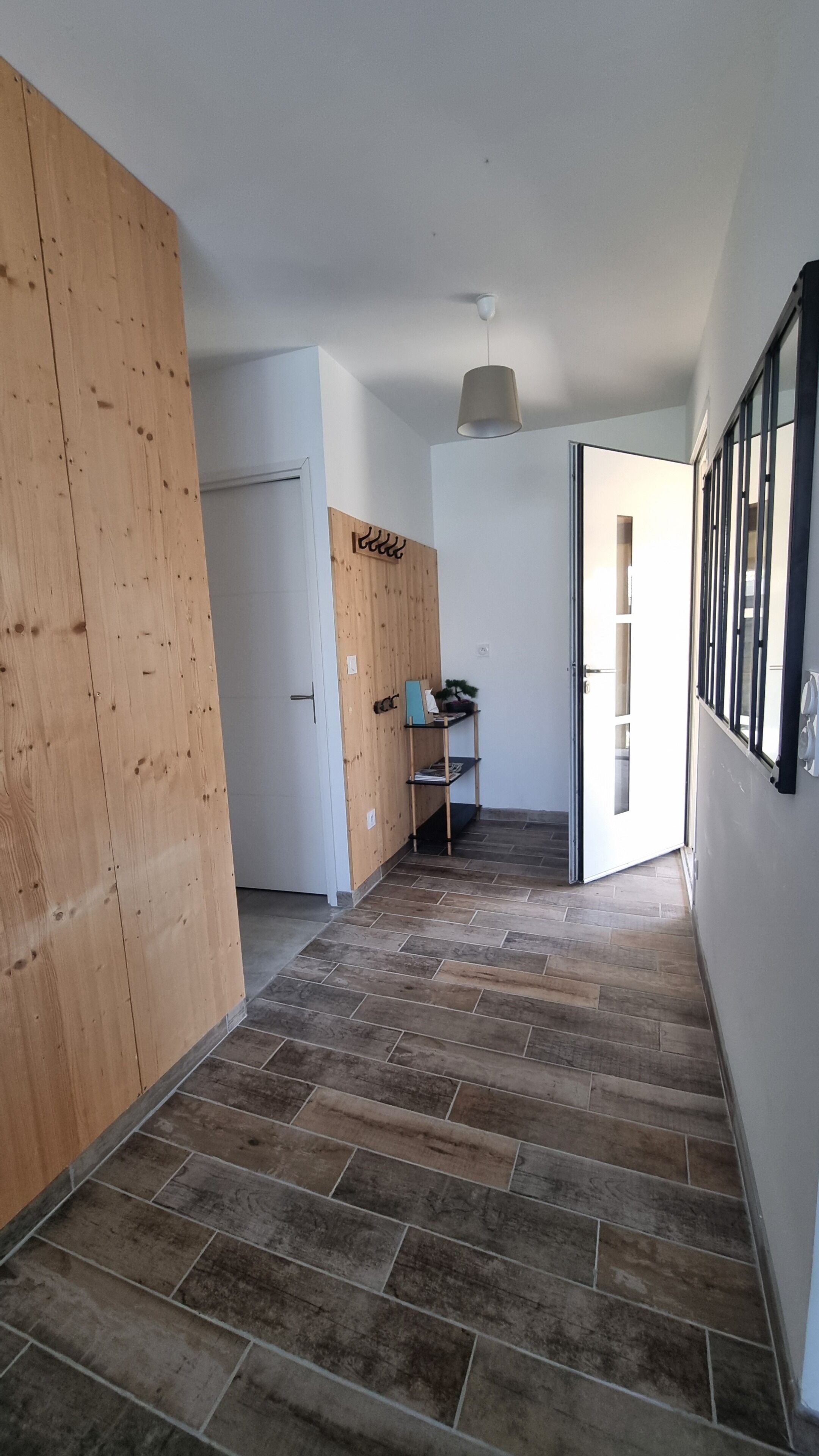 Um corredor com paredes de madeira, piso ladrilhado, um porta-roupas e uma porta que dá para outro quarto.