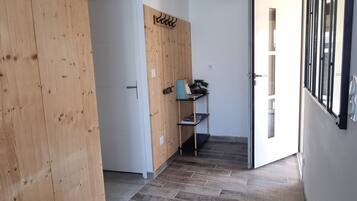 Um corredor com paredes de madeira, piso ladrilhado, um porta-roupas e uma porta que dá para outro quarto.