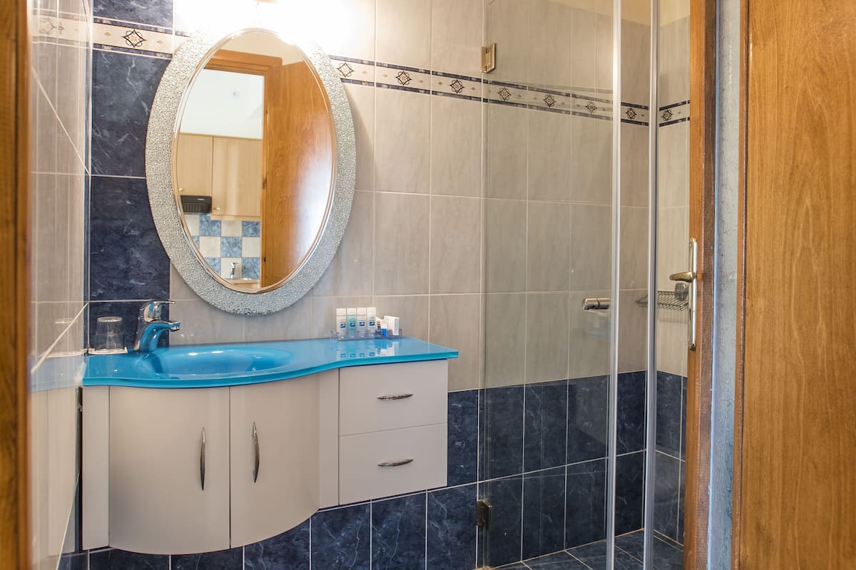 Casa de banho com lavatório azul, espelho redondo e cabine de duche em vidro.