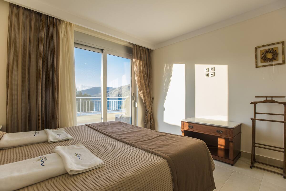 Quarto de hotel com cama, escrivaninha, guarda-roupa e vista para as montanhas pela janela.