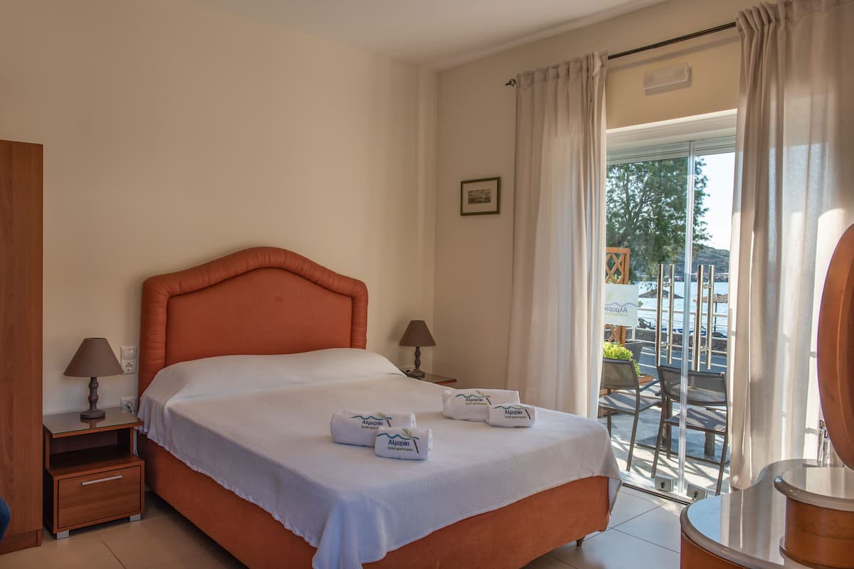 Quarto de hotel com uma cama grande, duas mesas de cabeceira com luminárias, uma gaveta pequena e vista para a área externa através de uma porta de vidro deslizante.