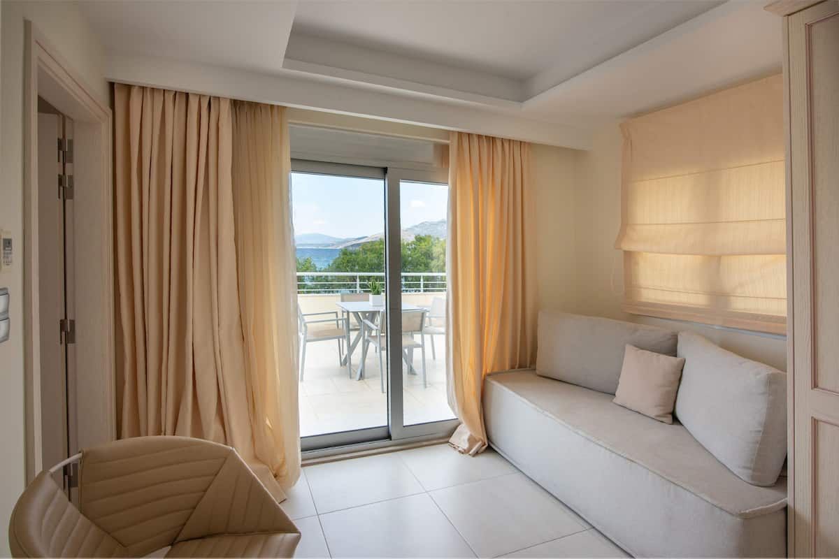 Uma sala de estar moderna com um sofá, uma poltrona e uma porta de vidro deslizante que dá para uma área externa com mesa e cadeiras.