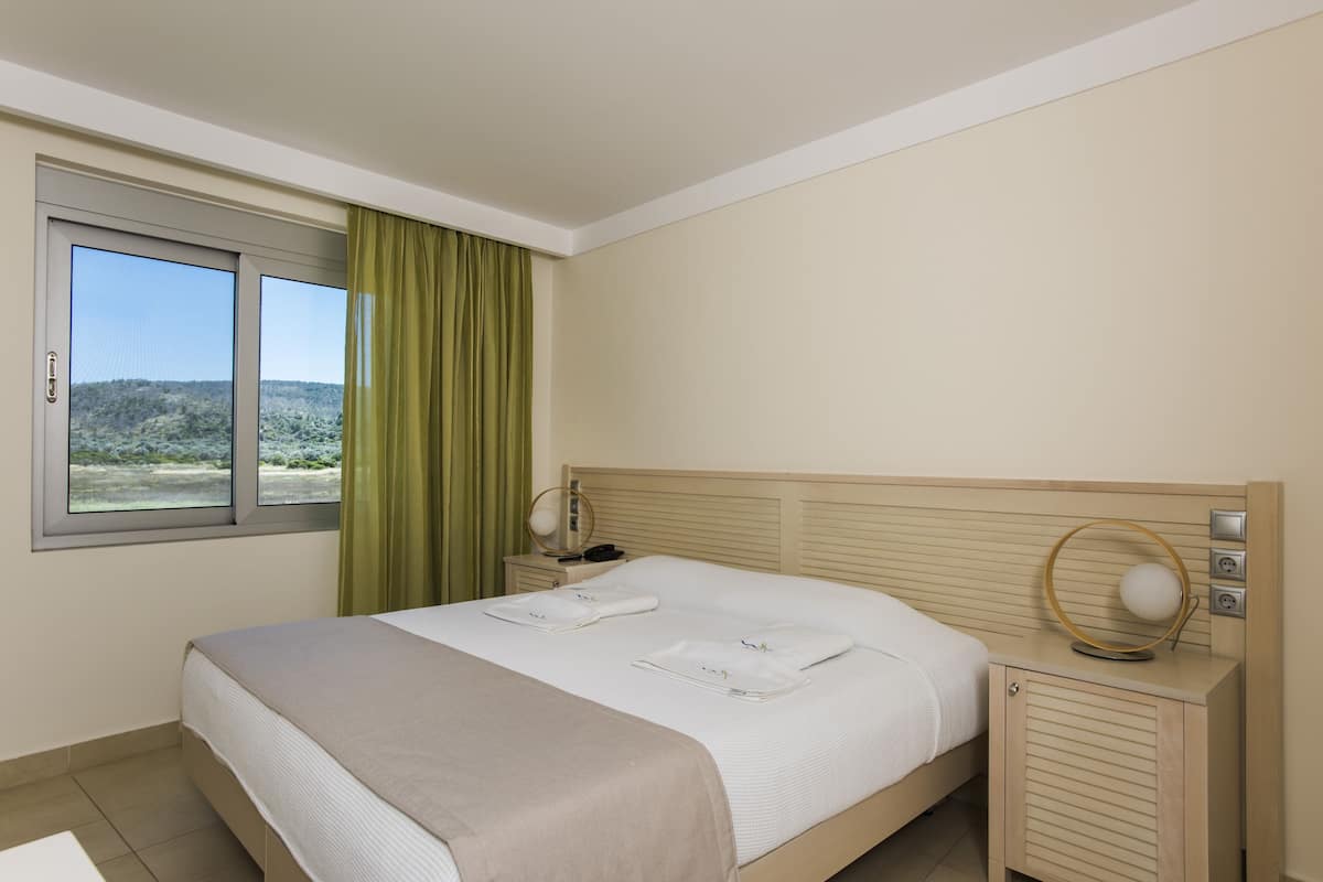 Quarto de hotel com cama, mesa de cabeceira, luminária e vista para o exterior.