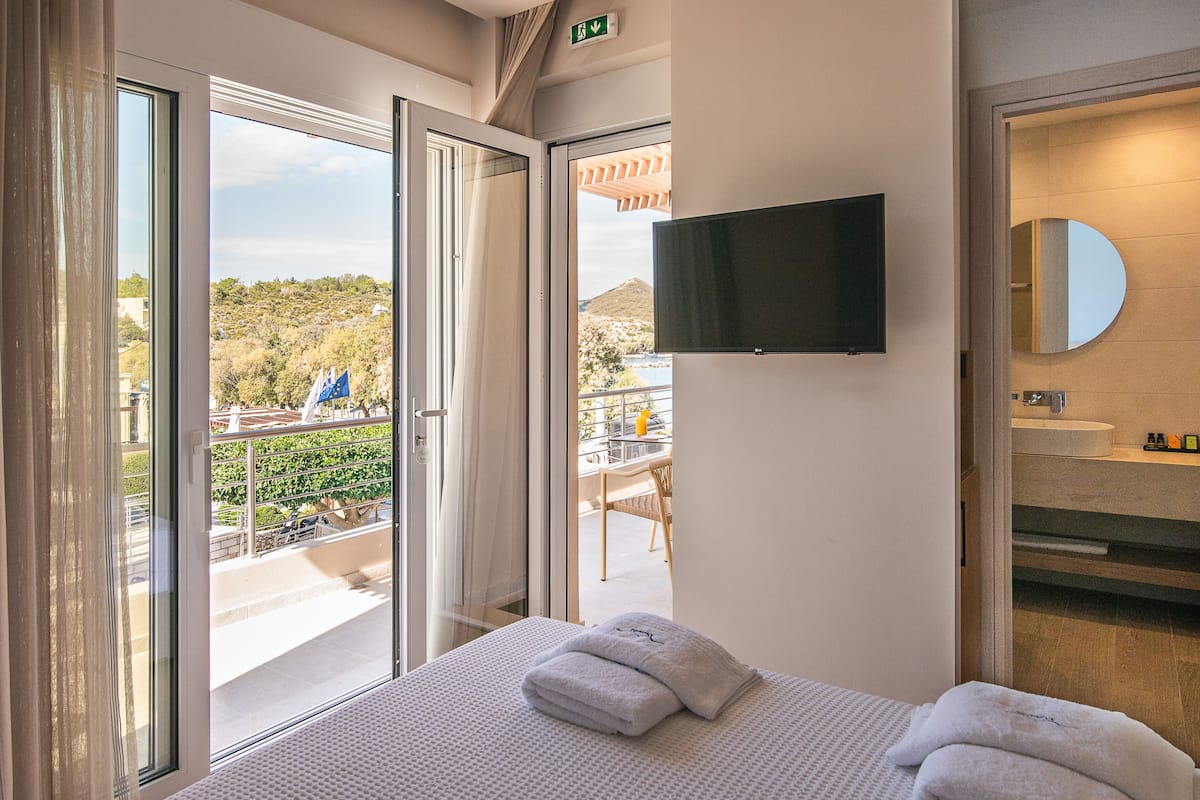 Quarto de hotel com cama, televisão, banheiro com pia e varanda com vista para a paisagem.