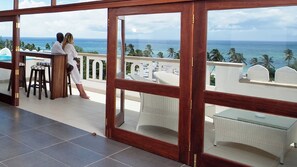 Uma varanda com vista para o oceano, móveis de vime branco e piso de azulejos.