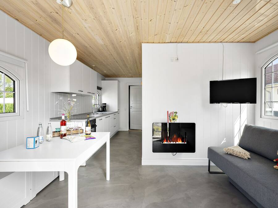 Uma sala de estar moderna com lareira, uma televisão de tela plana, um sofá e uma área de jantar com uma mesa branca.
