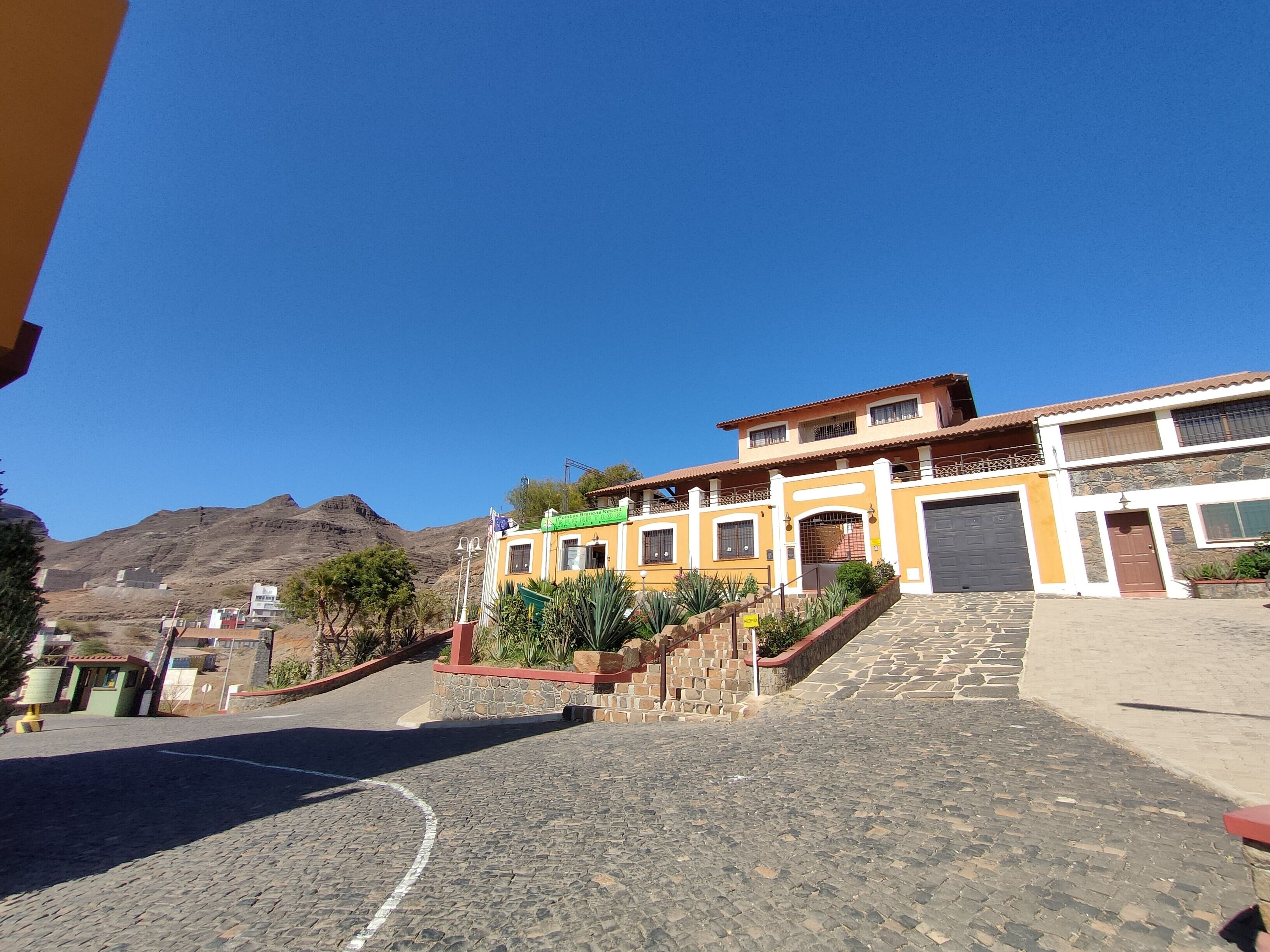 Um edifício de dois andares com uma escadaria de pedra que leva à entrada, uma garagem e uma montanha ao fundo.