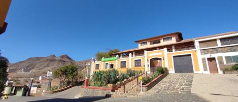 Um edifício de dois andares com uma escadaria de pedra que leva à entrada, uma garagem e uma montanha ao fundo.