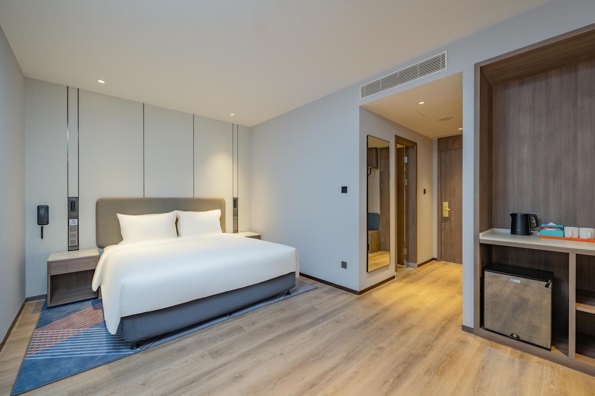 Quarto de hotel moderno com cama, mesa de cabeceira e um pequeno frigorífico.