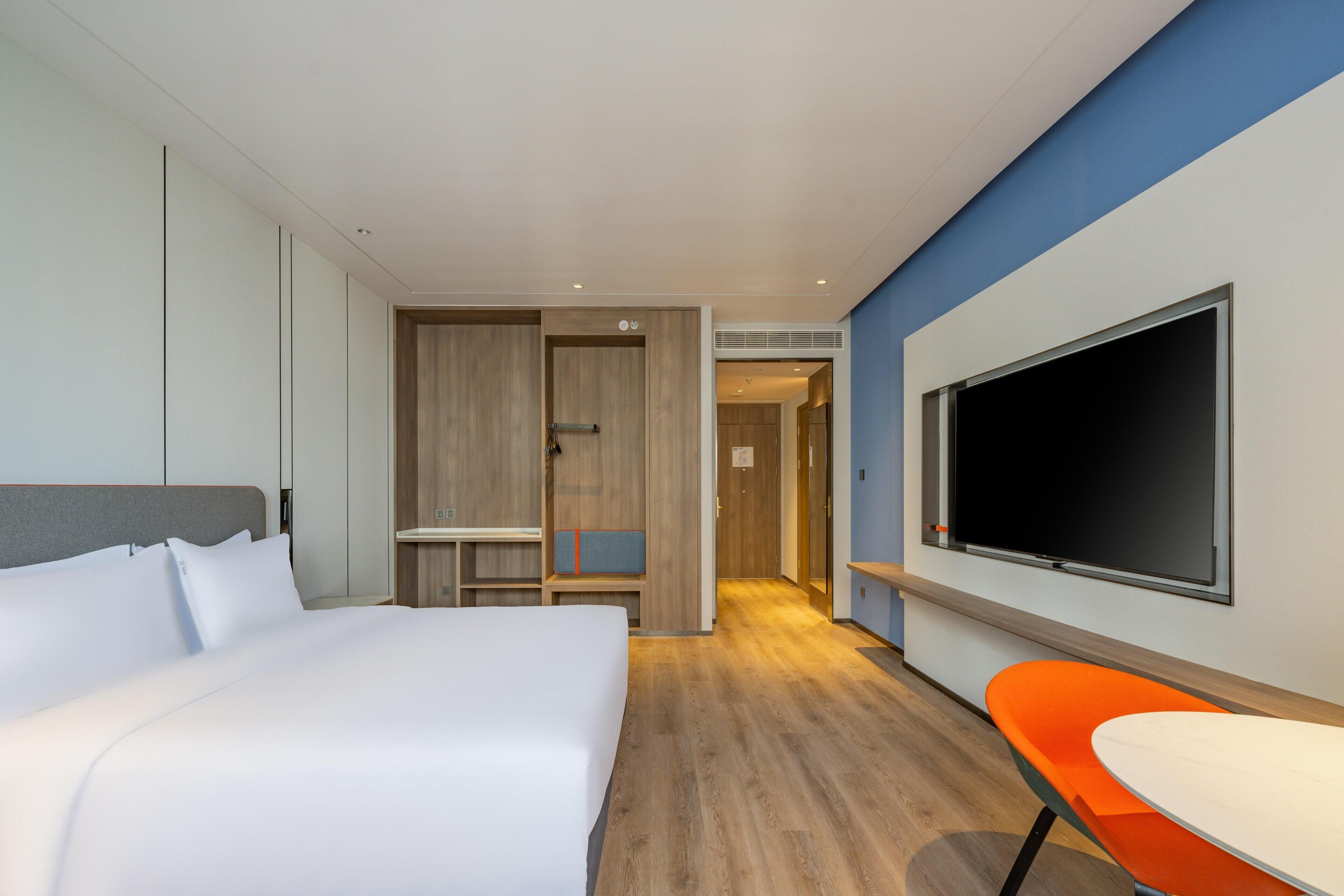 Quarto de hotel moderno com uma cama grande, uma televisão, uma escrivaninha e uma cadeira.