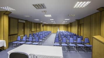 Uma sala de conferências com fileiras de cadeiras, uma mesa longa e painéis de madeira nas paredes.