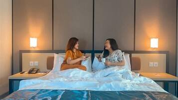 Quarto de hotel com uma cama grande, duas mesas de cabeceira e luminárias fixadas na parede.