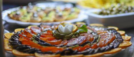 Diversos pratos em uma mesa de buffet, incluindo uma tarte com tomate e alcachofras.