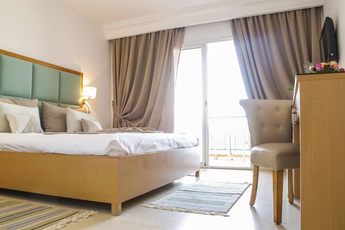 Quarto de hotel com cama, escrivaninha, cadeira e vista para o exterior.