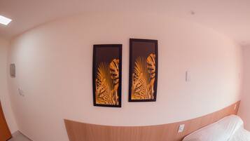 Quarto de hotel com parede curva, cabeceira de madeira e duas obras de arte emolduradas.