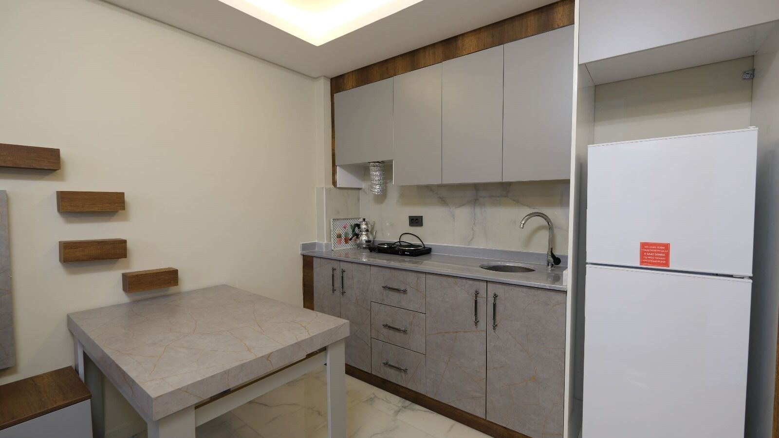 Uma cozinha compacta com bancada de mármore, pia embutida e frigorífico branco.