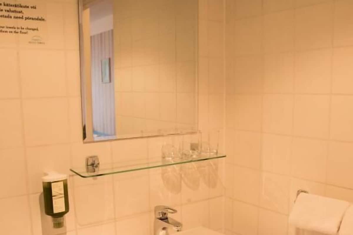 Casa de banho com lavatório branco, uma prateleira de vidro acima, espelho e porta-toalhas.