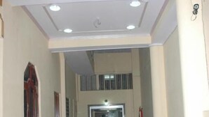 Um saguão de hotel com piso de mármore, plantas em vasos, tapete vermelho e uma grande porta de vidro que dá para a entrada.