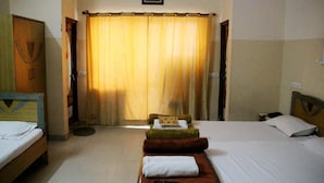 Quarto de hotel com uma cama, cabeceira de madeira, uma mesa pequena com um controle remoto e uma cortina ao fundo.