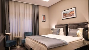 Quarto de hotel com uma cama grande, duas cadeiras, uma mesinha e um quadro na parede.
