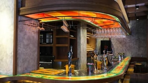Uma área de bar com balcão curvo, várias torneiras e copos pendurados.