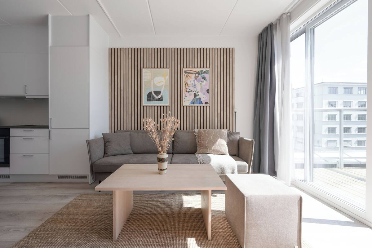 Uma sala de estar moderna com um sofá, uma mesa de centro e vista para a cidade através de grandes janelas.