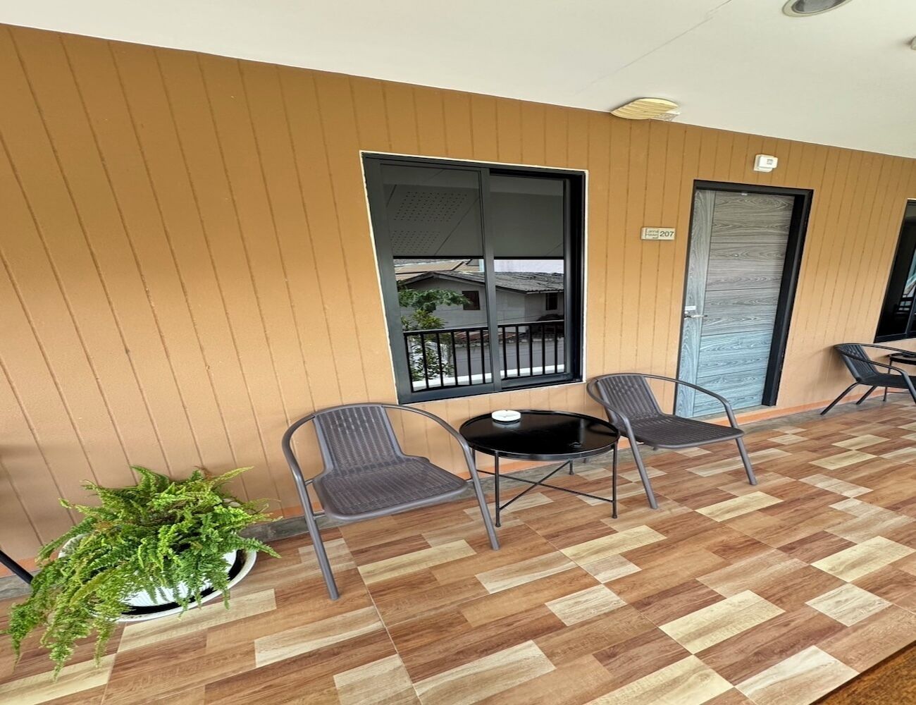 Um quarto com piso xadrez, duas cadeiras, uma mesinha e um vaso de planta.