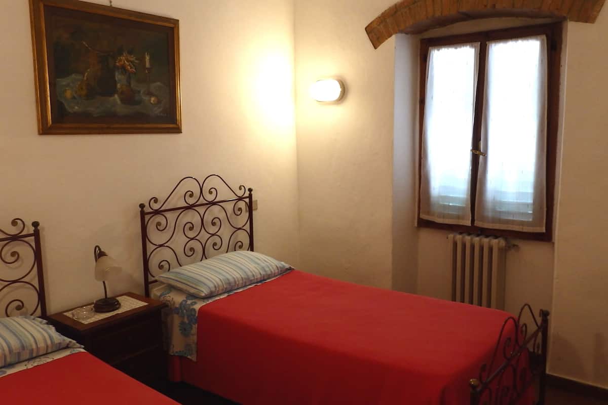 Quarto com duas camas, um quadro na parede, uma janela com cortinas e um radiador.