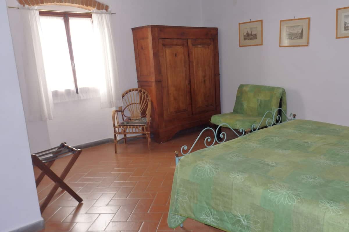 Quarto com cama, guarda-roupa de madeira, cadeira e janela com cortinas.