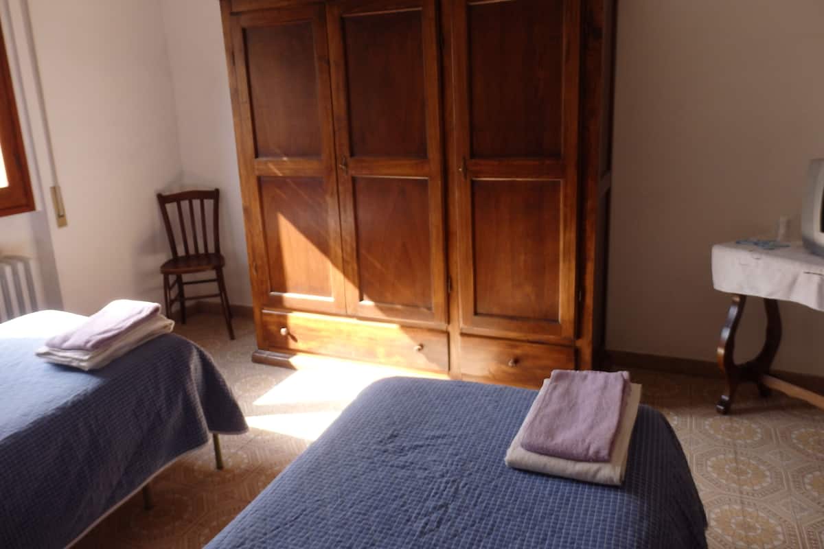 Quarto com duas camas, um guarda-roupa de madeira, uma cadeira e uma mesa pequena com televisão.